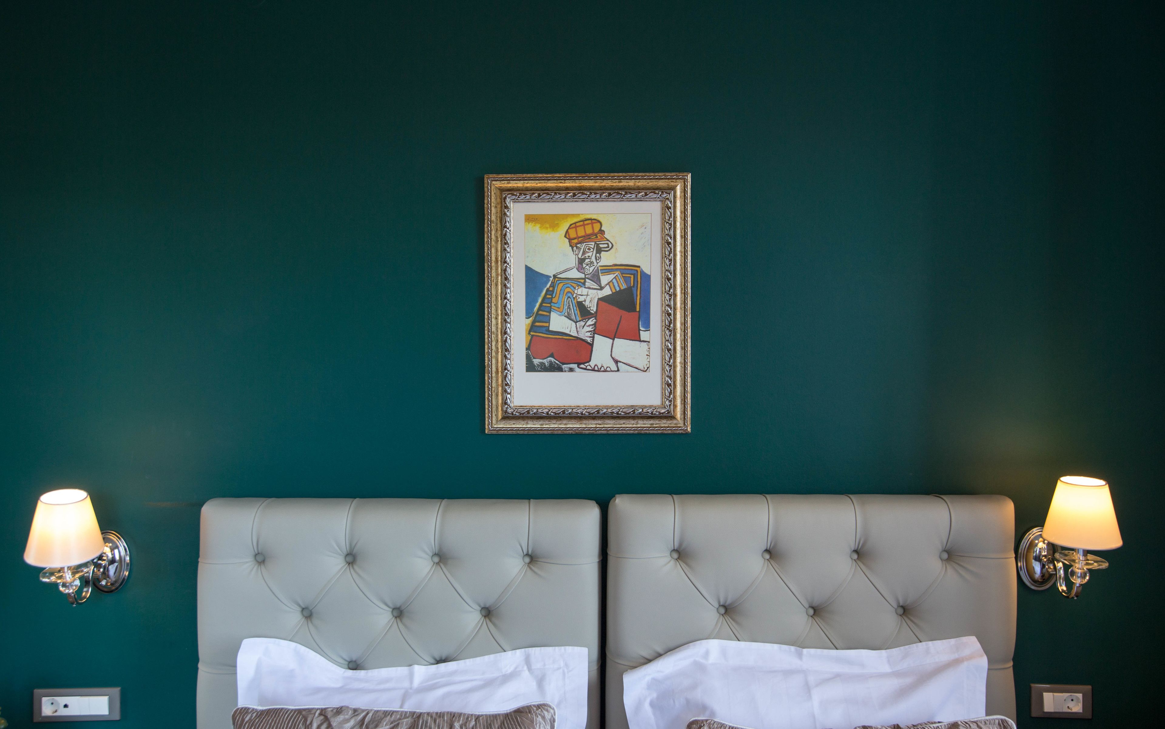 Quarto com duas camas, cada uma com cabeceira estofada e roupa de cama branca. Luminárias fixadas na parede em ambos os lados das camas. Uma obra de arte emoldurada pendurada na parede acima das camas.