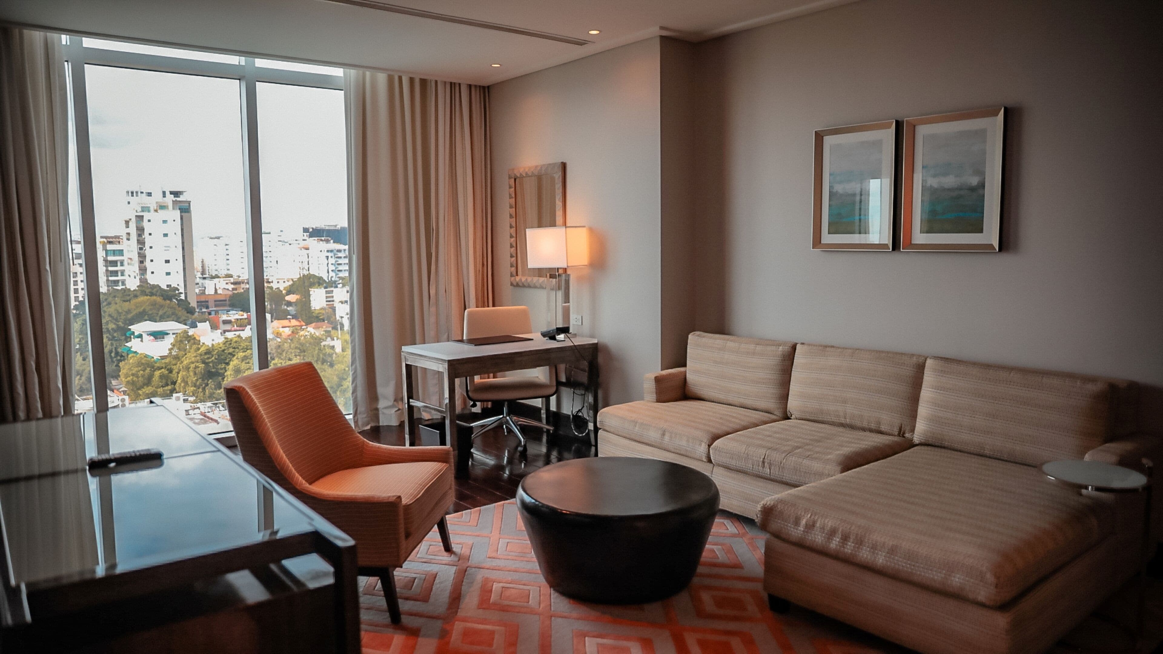 Quarto de hotel com uma janela grande, um sofá, uma cadeira, uma escrivaninha e um abajur.