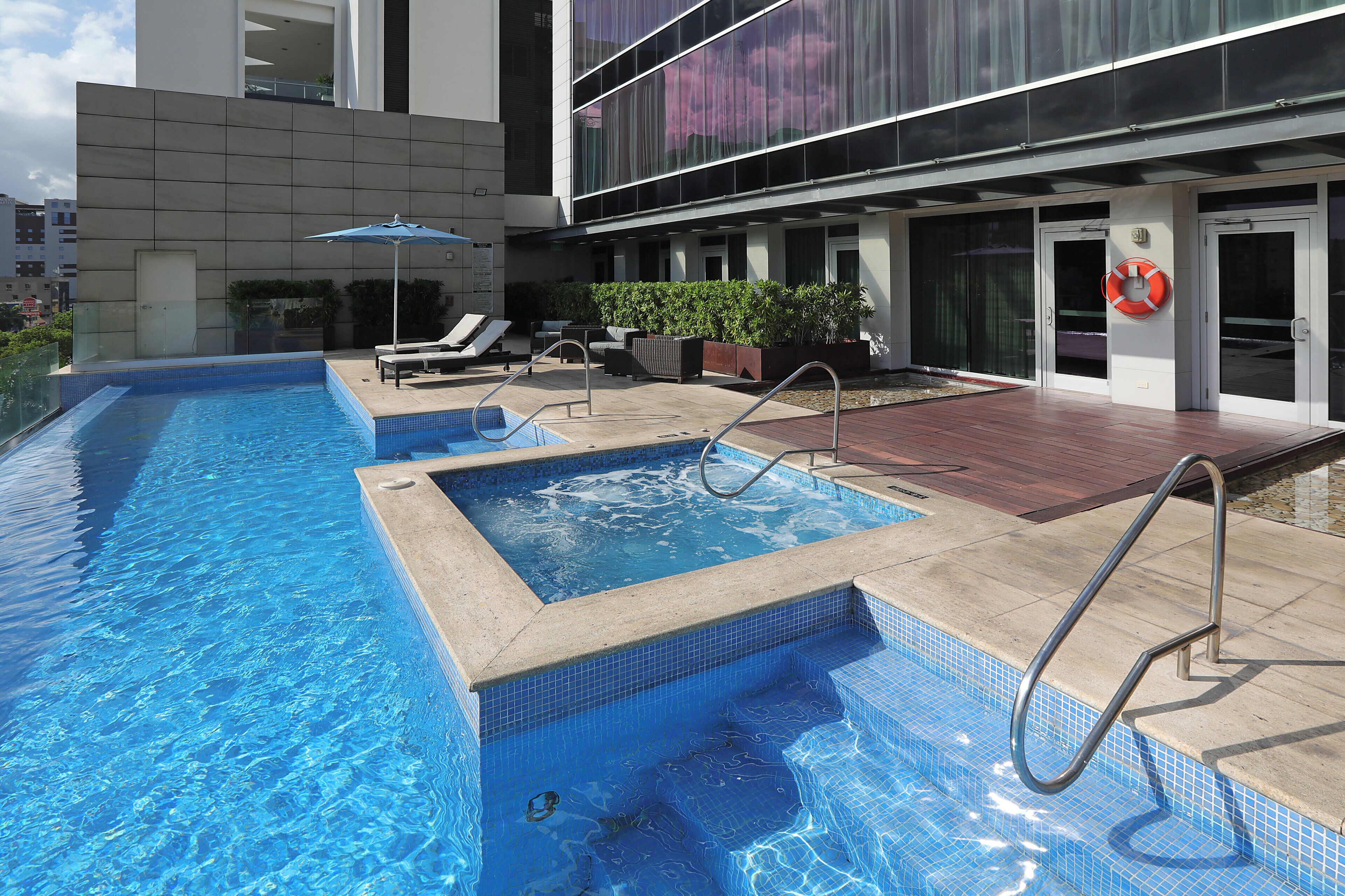 Uma piscina com plataforma de mergulho, espreguiçadeiras e um flutuador na parede.