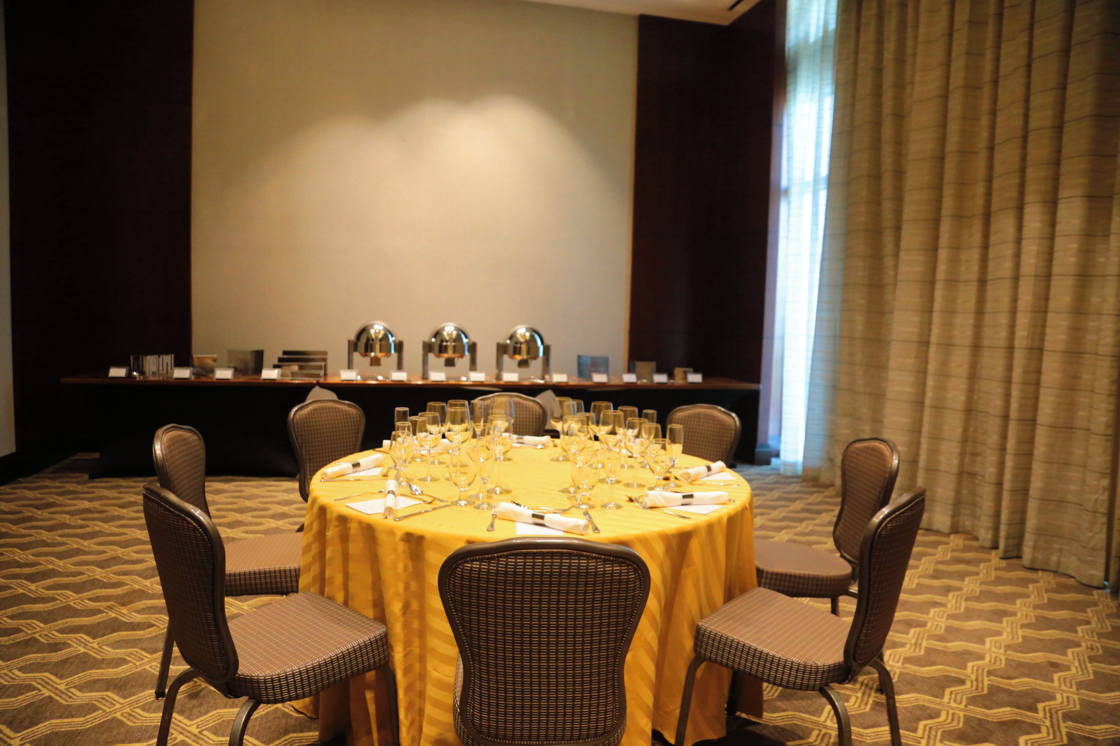 Uma sala de conferência com uma mesa redonda preparada para uma reunião, cercada por cadeiras.
