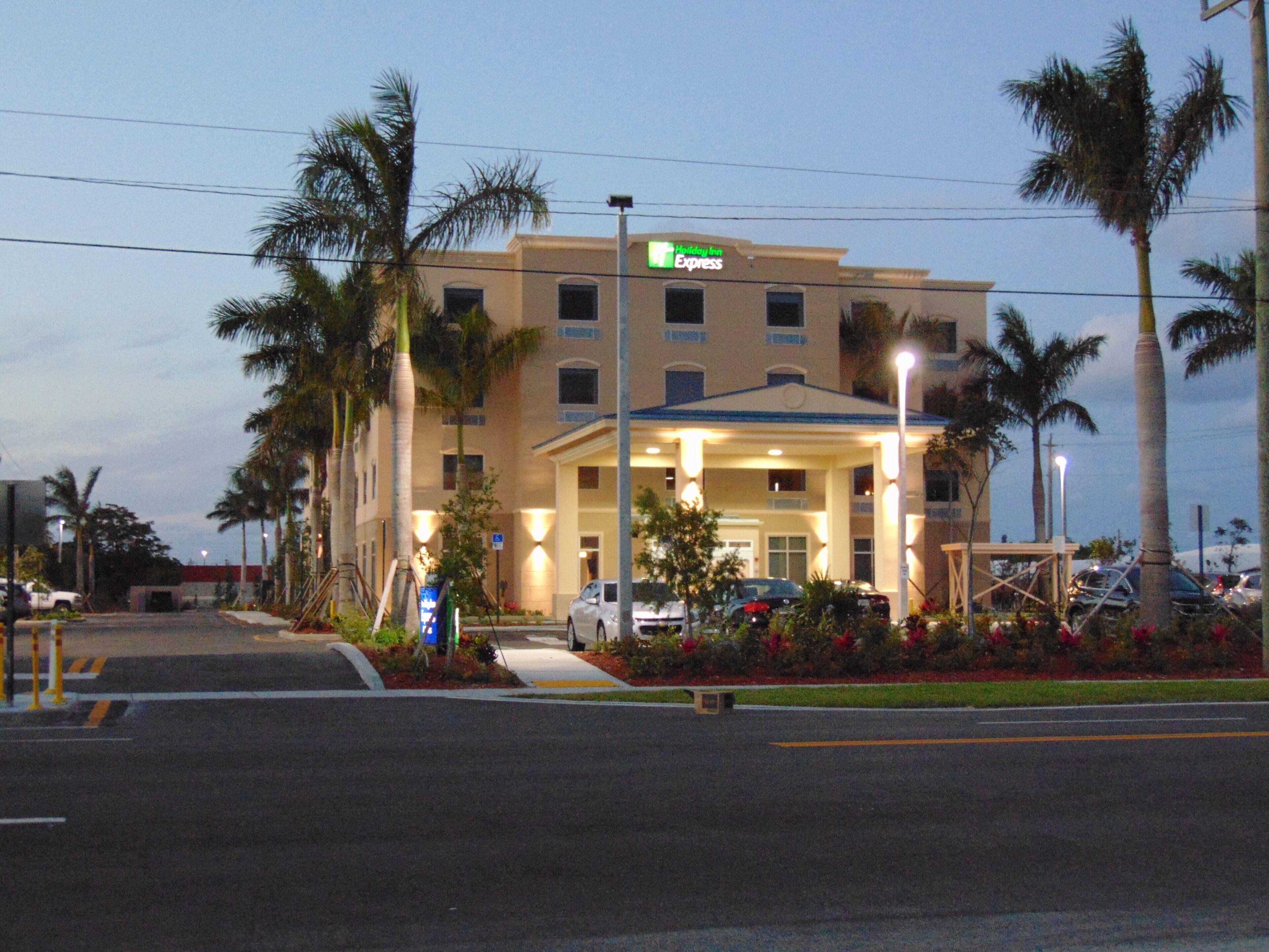 Edifício Holiday Inn Express com entrada coberta, palmeiras e estacionamento.