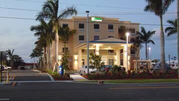 Edifício Holiday Inn Express com entrada coberta, palmeiras e estacionamento.