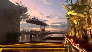 Um deck de madeira com piscina, área de estar externa e plantas tropicais.