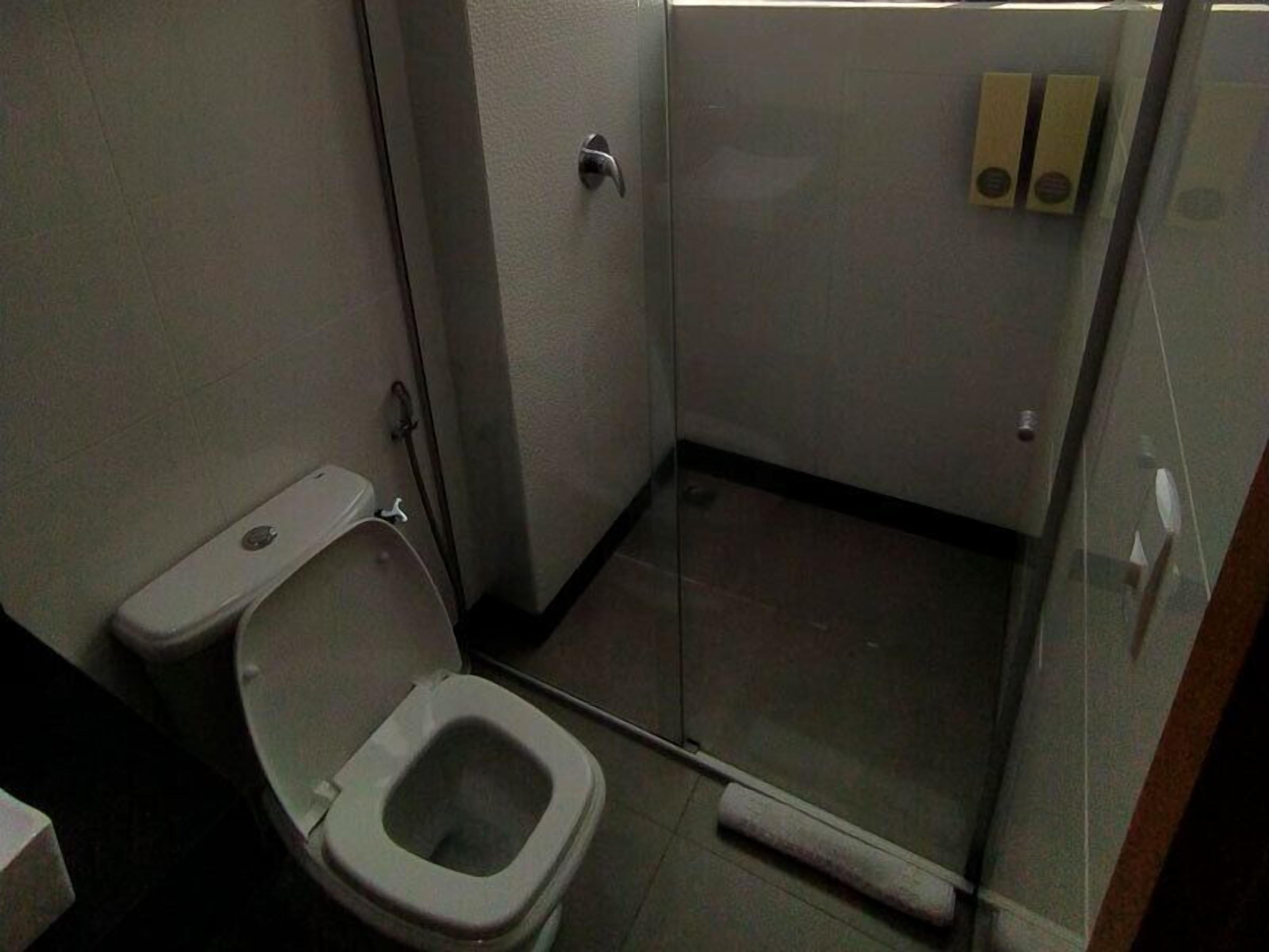Casa de banho pequena e fechada, com sanita, cabine de duche e dispensador de papel higiénico.