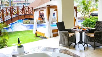 Varanda com vista para uma piscina, cama com dossel, cadeiras de vime e mesa de café da manhã.