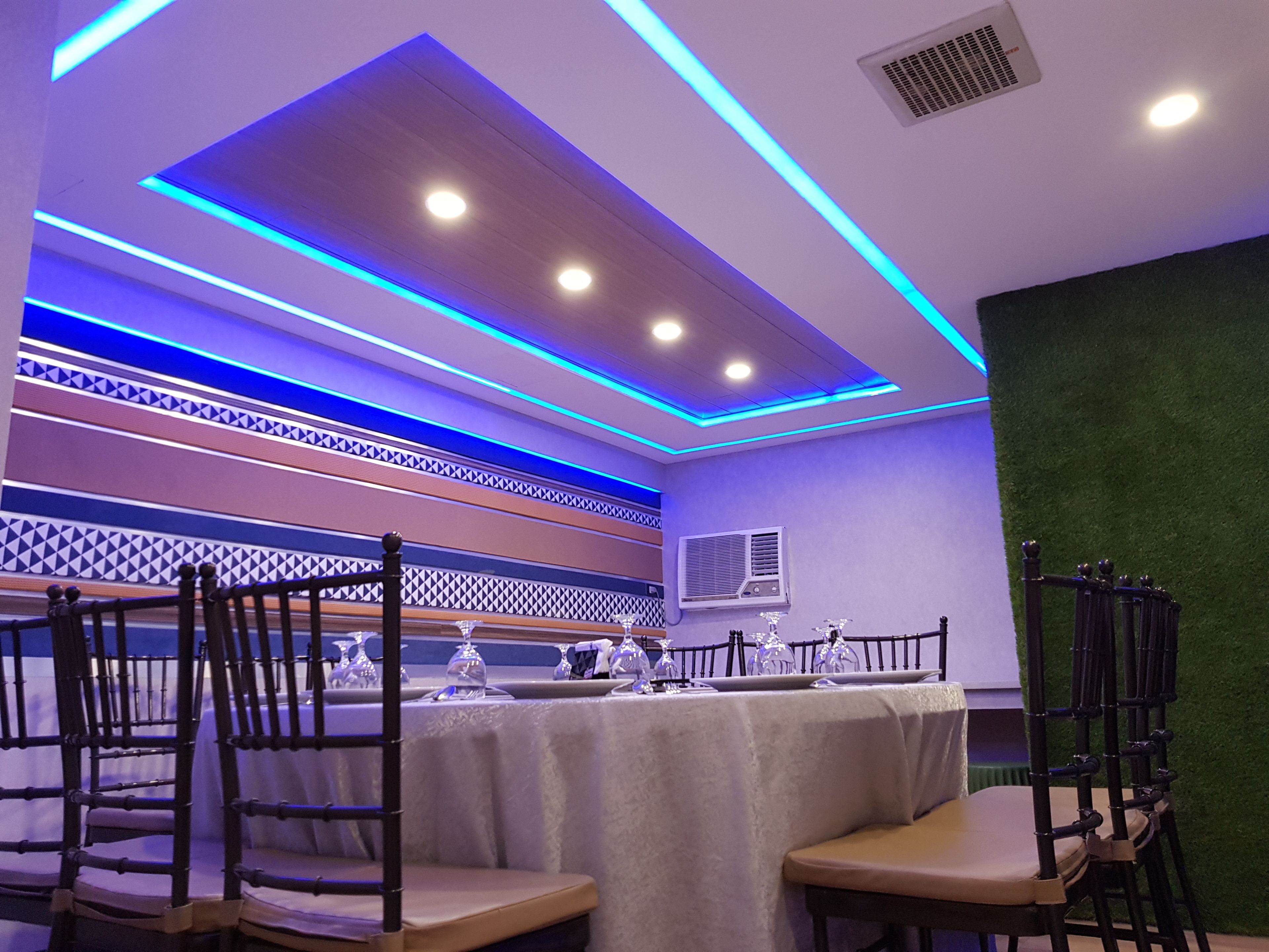 Uma área de refeições com uma mesa posta para quatro pessoas, cadeiras e teto com iluminação azul em LED.