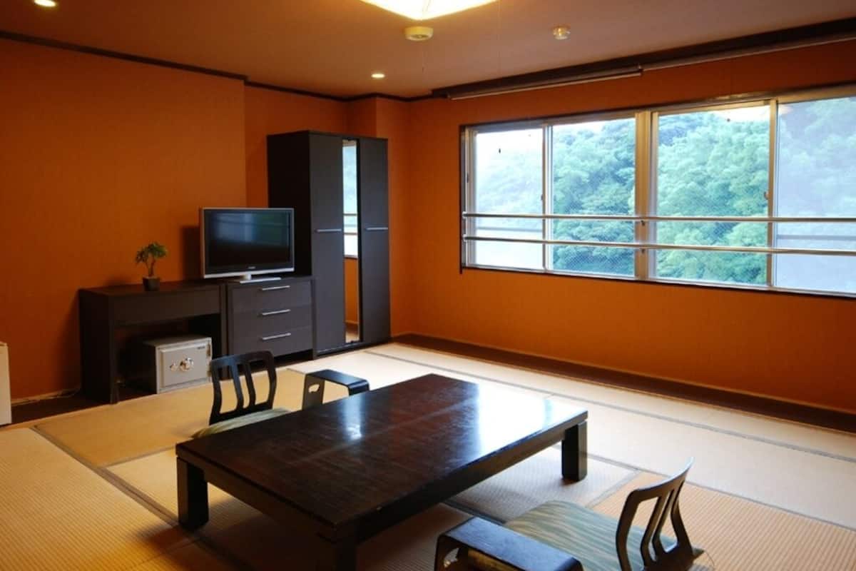 Um quarto japonês tradicional com tatames, uma mesa baixa e uma televisão sobre um móvel.