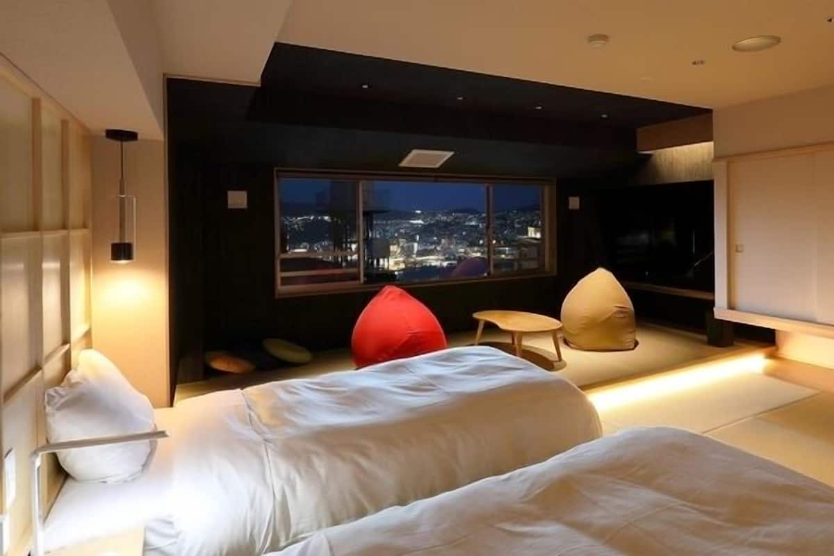Quarto de hotel moderno com vista para a cidade, uma cama, uma cadeira vermelha e uma mesa pequena.