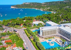 Resort com uma piscina grande, praia e montanhas ao fundo.