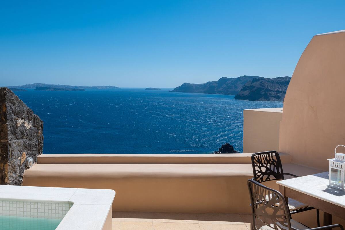 Varanda com vista para o mar, uma piscina e uma mesa com cadeiras.