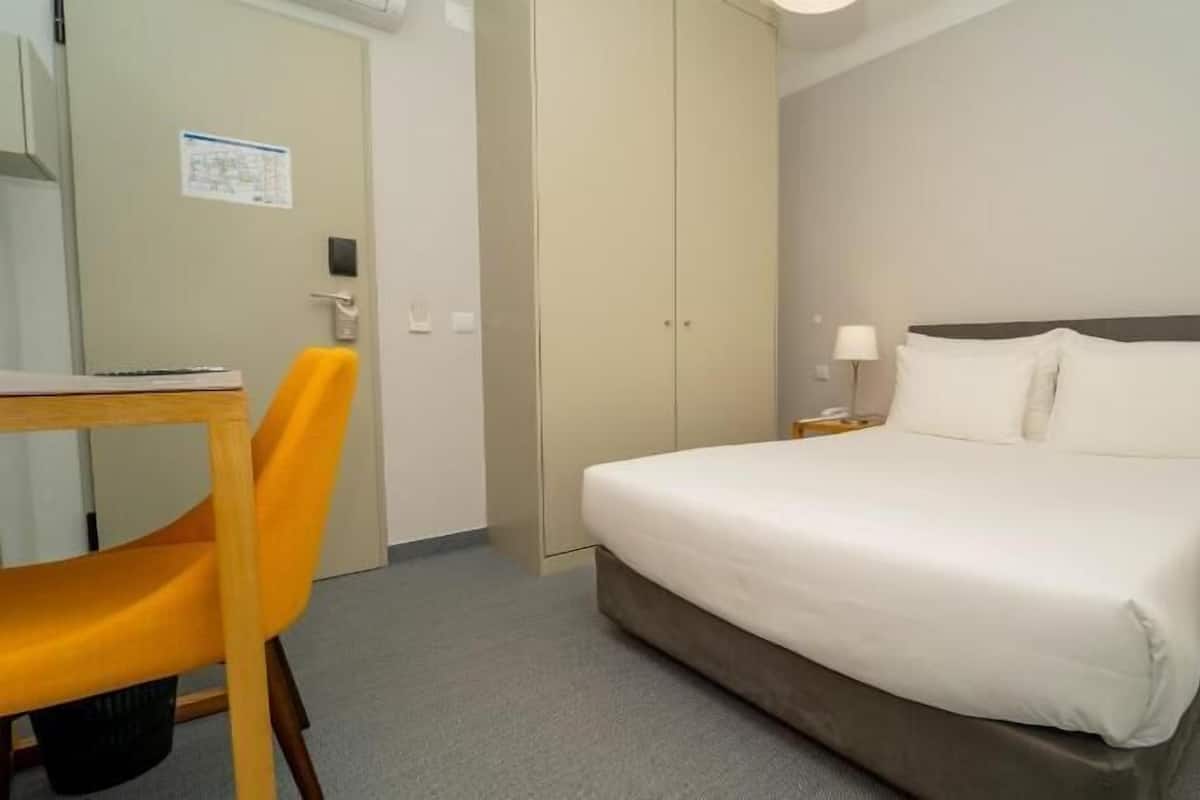 Quarto de hotel com uma cama, uma escrivaninha, uma cadeira e duas mesas de cabeceira com luminárias.