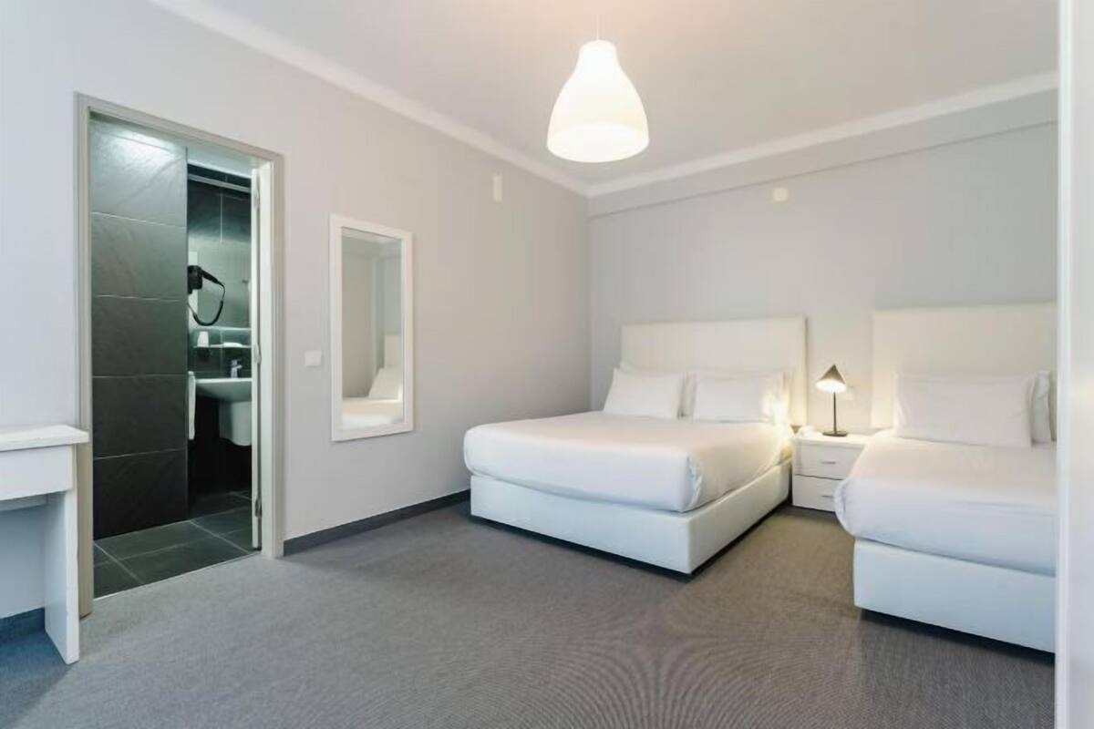 Quarto de hotel com cama, mesa de cabeceira, abajur e espelho.