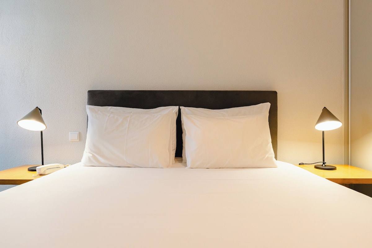 Quarto de hotel com cama grande, duas luminárias de cabeceira e telefone ao lado da cama.