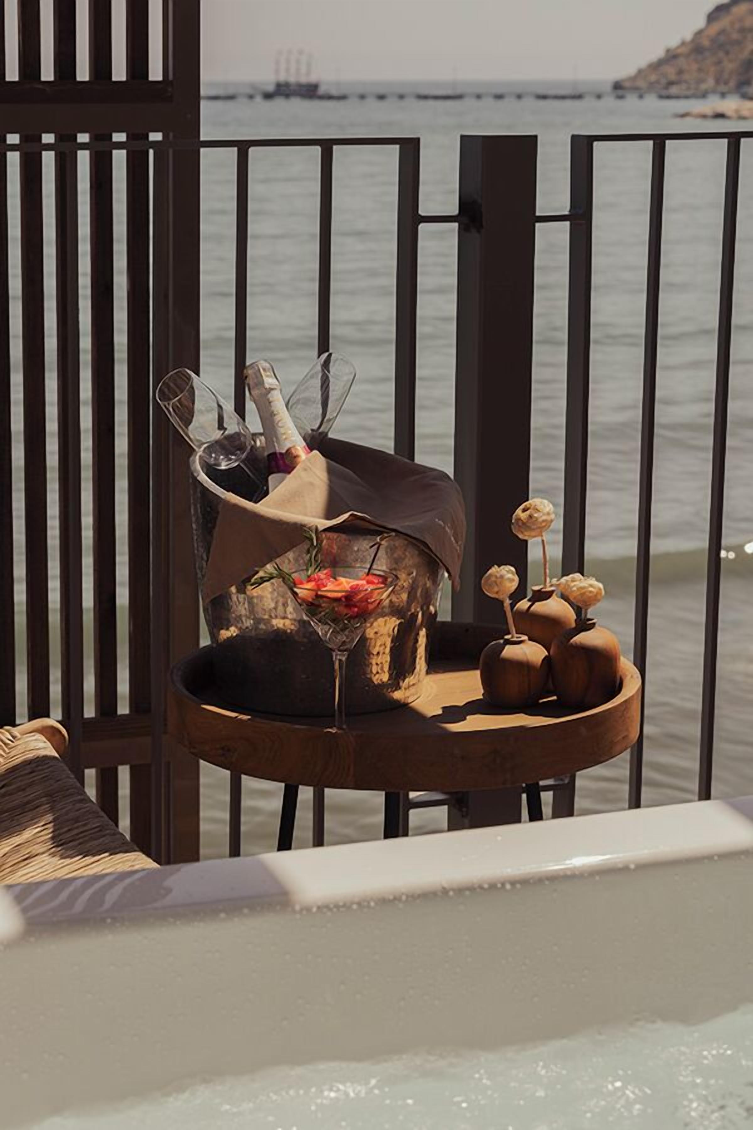 Uma cadeira de madeira com uma garrafa de vinho, copos e objetos decorativos à beira de uma piscina, com vista para o mar.