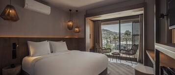 Quarto de hotel moderno com uma cama grande, uma varanda com cadeiras de vime e vista para a cidade.