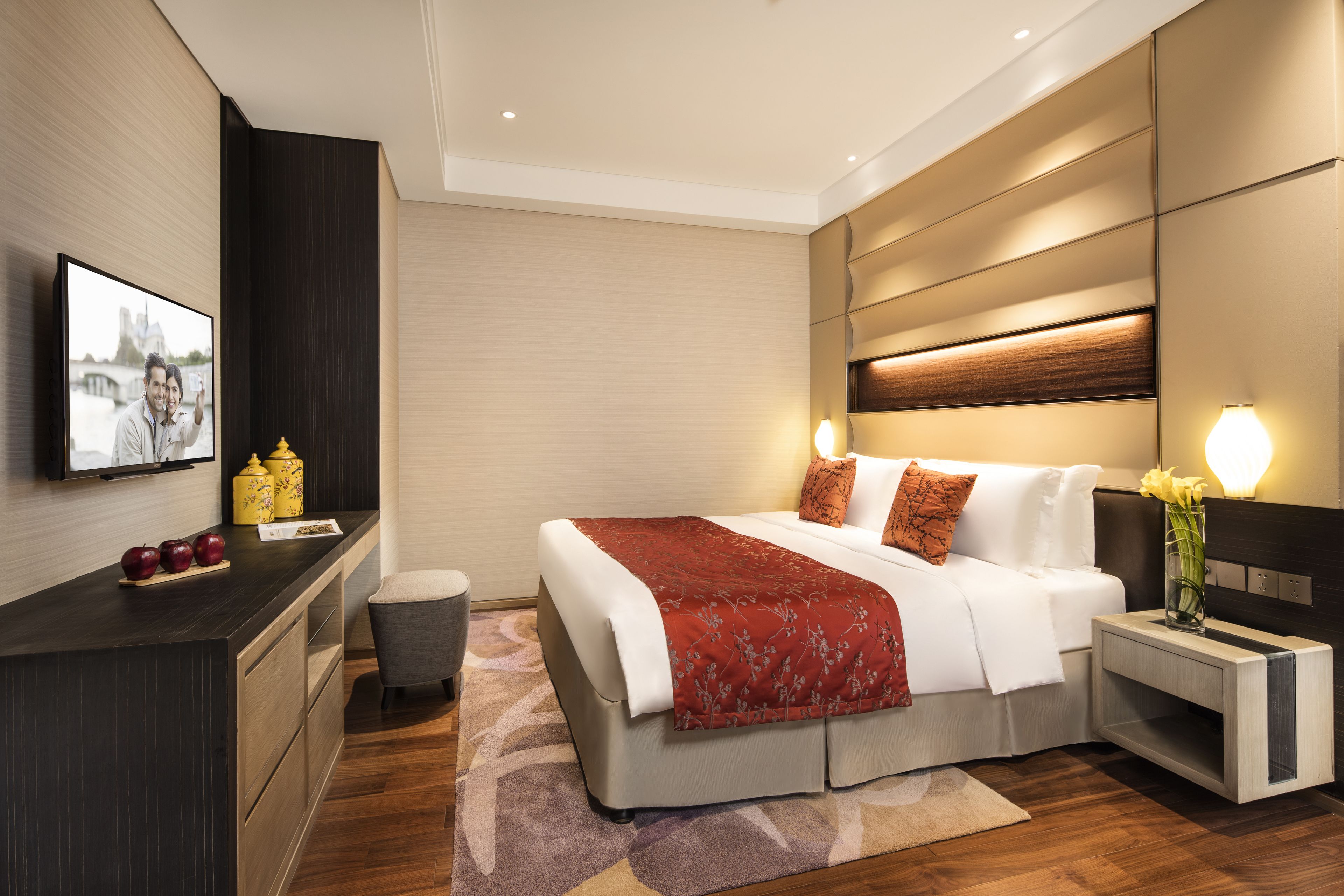Quarto de hotel moderno com uma cama grande, mesas de cabeceira, escrivaninha e televisão de tela plana na parede.