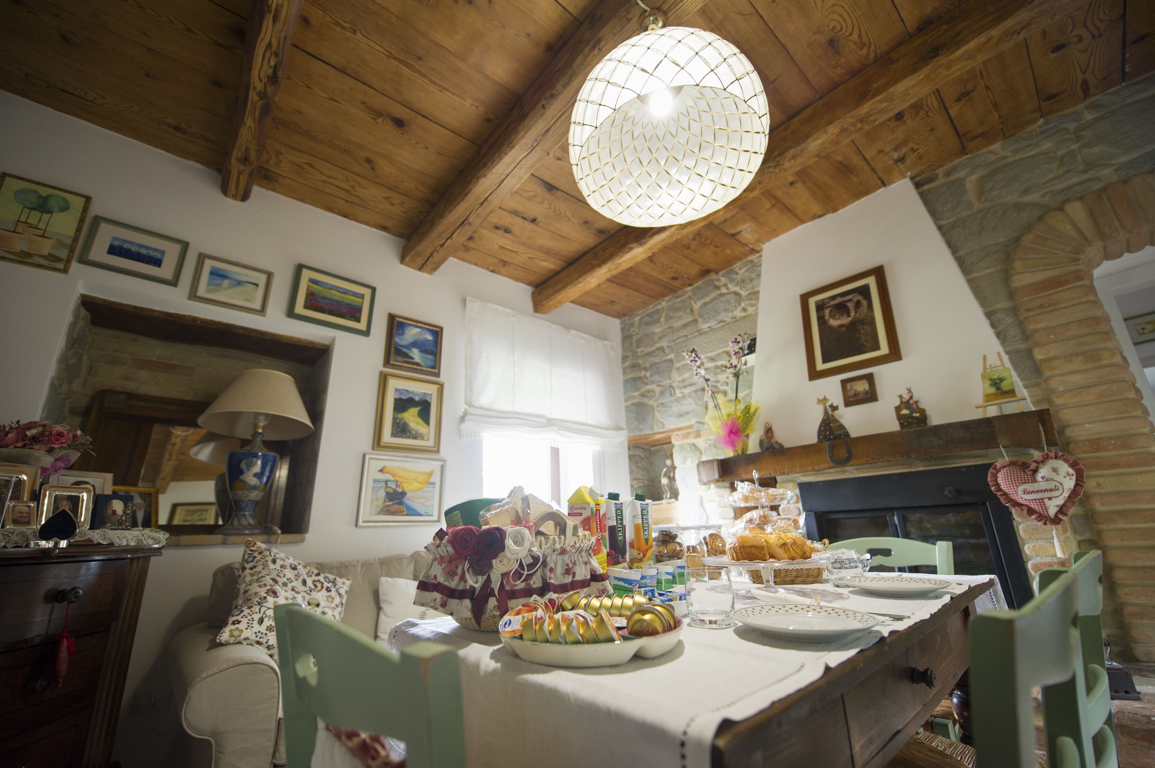 Uma sala de jantar rústica com uma mesa de madeira posta para refeição, cercada por paredes de pedra e vigas de madeira.