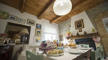 Uma sala de jantar rústica com uma mesa de madeira posta para refeição, cercada por paredes de pedra e vigas de madeira.
