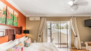 Quarto de hotel com cama, ventoinha no teto, televisão e varanda com cortinas.