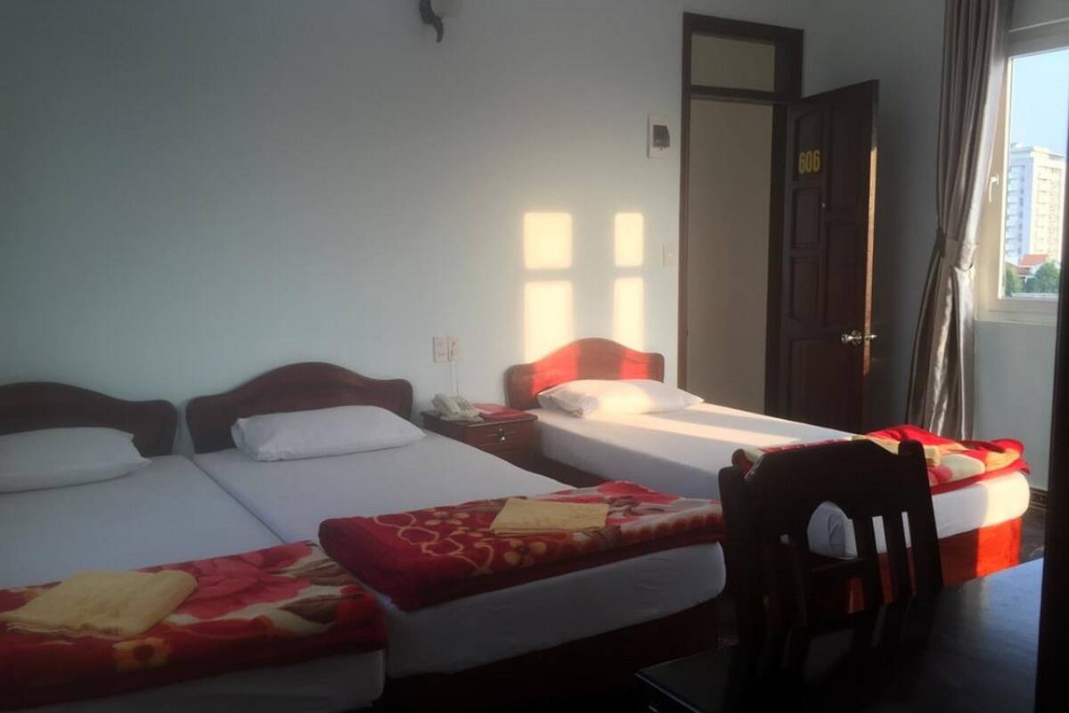 Quarto de hotel com duas camas de solteiro, uma escrivaninha e uma cadeira.