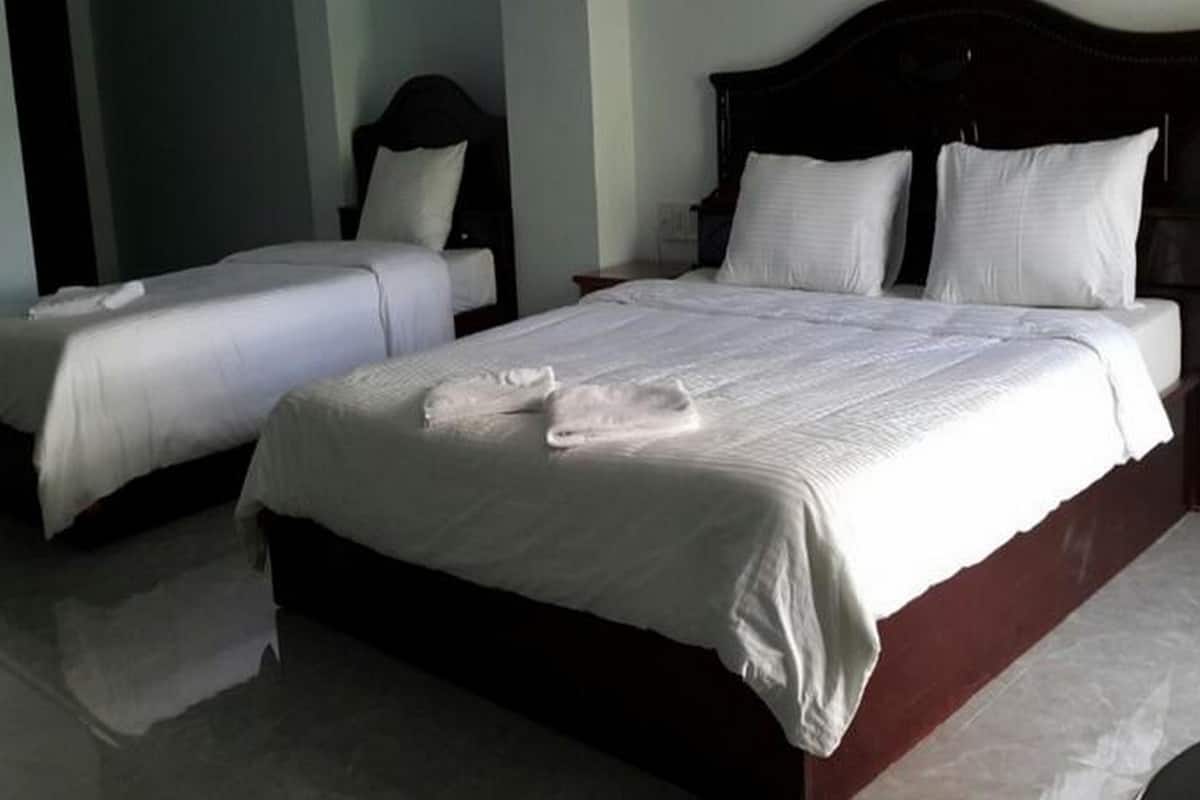 Quarto de hotel com duas camas de solteiro, cada uma com roupa de cama e almofadas brancas, e uma cama de casal com configuração similar.