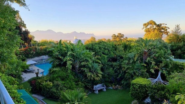 Um jardim exuberante com piscina, cercado por vegetação densa e montanhas ao fundo.