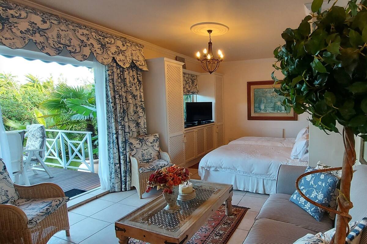 Um quarto com cama, televisão, janela com cortinas, planta e sofá.