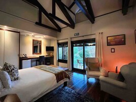 Quarto de hotel com cama, escrivaninha, cadeira e uma janela grande.