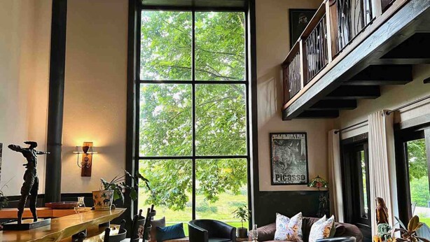 Um quarto amplo com uma grande janela, uma mesa de jantar de madeira e assentos confortáveis.