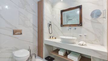 Um banheiro moderno com vaso sanitário branco, pia com bancada de mármore, aparador de madeira, espelho e porta-toalhas.