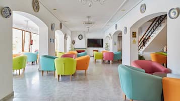 Um hall amplo com poltronas coloridas, um lustre e uma escadaria.