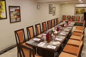 Uma sala de conferências com uma mesa comprida, cadeiras e obras de arte emolduradas nas paredes.