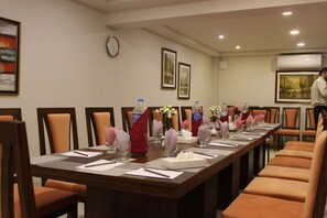 Uma sala de conferências com uma mesa comprida, cadeiras, garrafas de água e arranjos florais.