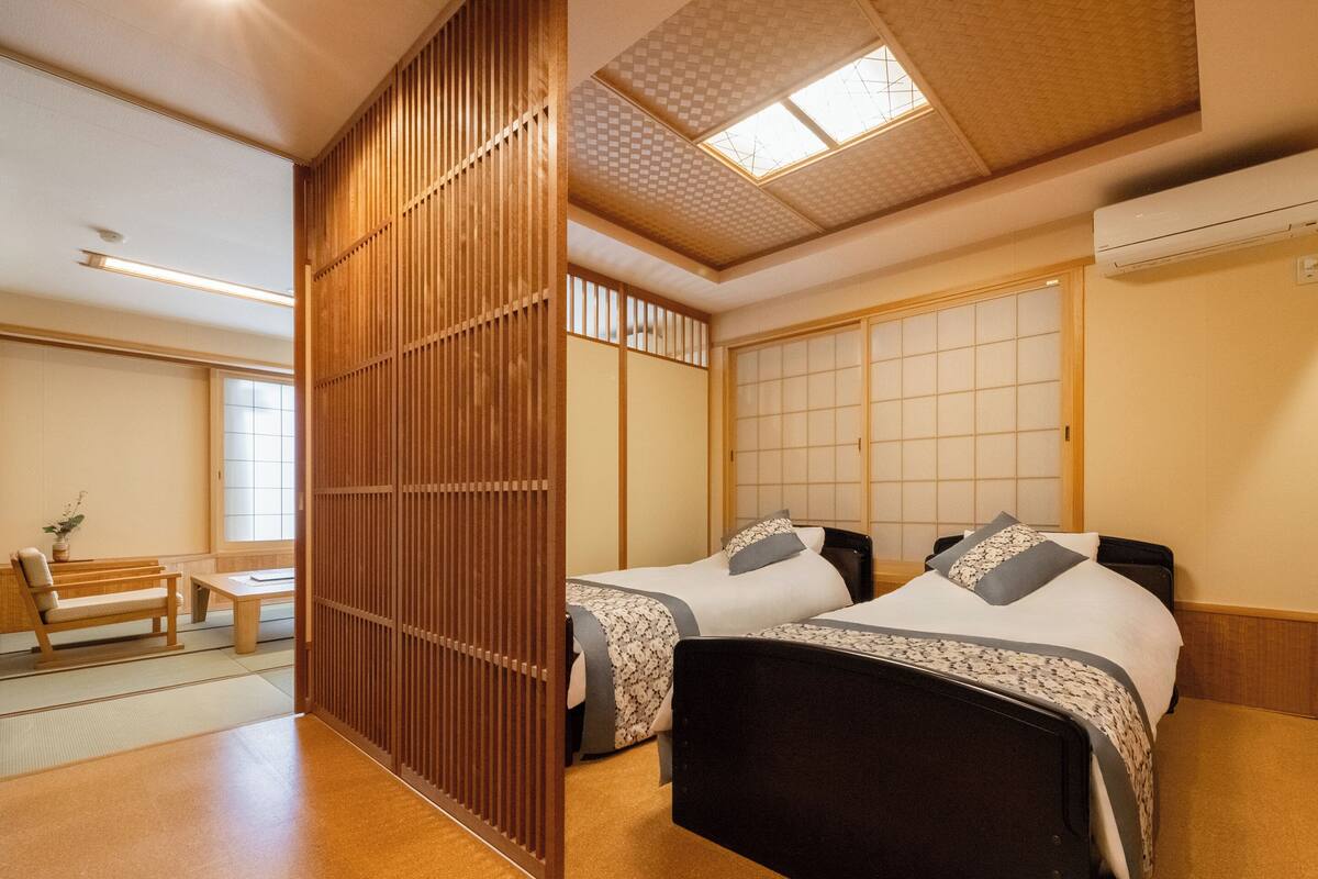 Quarto japonês tradicional com tatames, duas camas com roupa de cama floral, uma porta deslizante e um biombô shoji.