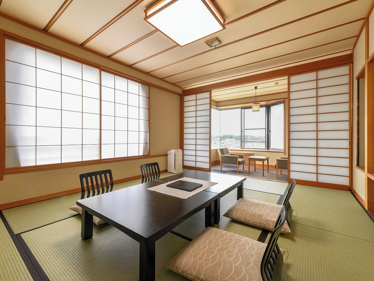 Um quarto em estilo japonês tradicional, com tatames, uma mesa baixa, cadeiras e portas deslizantes shoji.