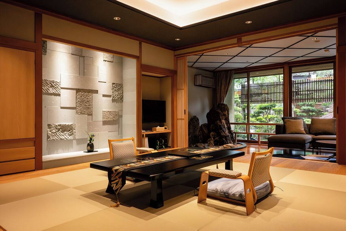 Quarto em estilo japonês tradicional, com tatames, uma mesa baixa e vista para um jardim através de grandes janelas.