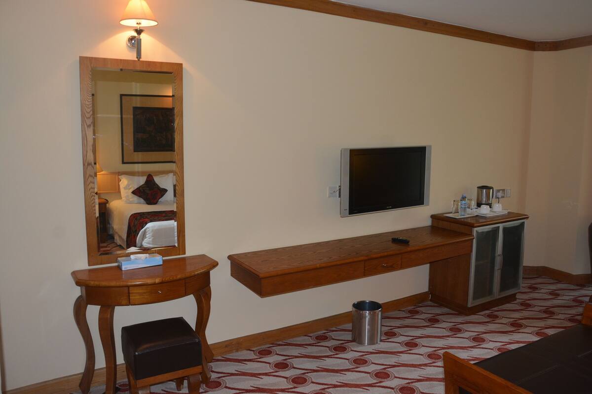 Quarto de hotel com secretária de madeira, televisão na parede, armário e chão estampado.