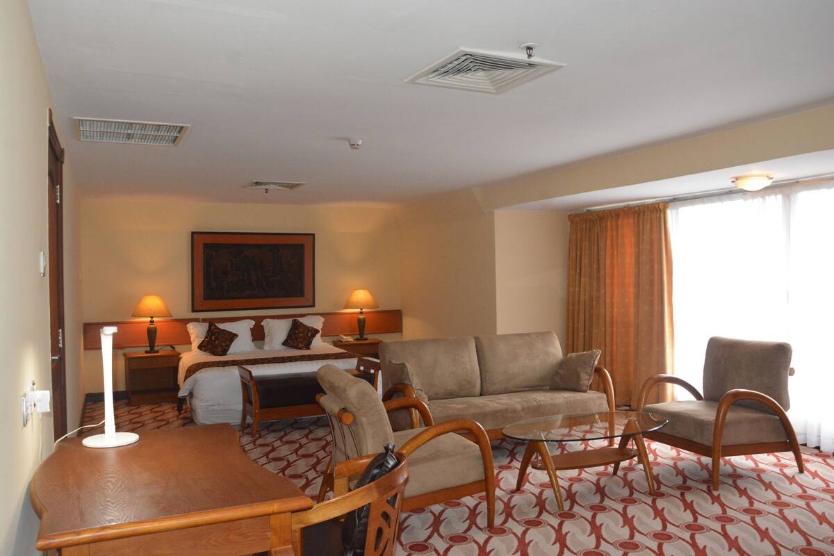 Quarto de hotel com cama, sofá, poltrona, mesa e abajur.