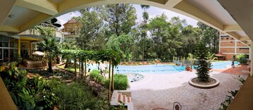 Uma área de piscina com um caminho pavimentado hexagonal, cercada por vegetação exuberante e um espaço coberto para sentar.