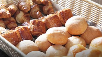 Uma cesta de vime repleta de produtos de panificação variados, incluindo croissants e pães redondos.