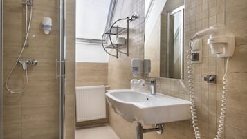 Casa de banho moderna com cabine de duche em vidro, lavatório branco e secador de cabelo embutido.