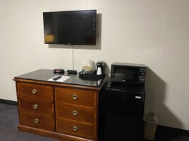 Quarto de hotel com penteadeira de madeira, televisão de tela plana na parede, cafeteira e micro-ondas.