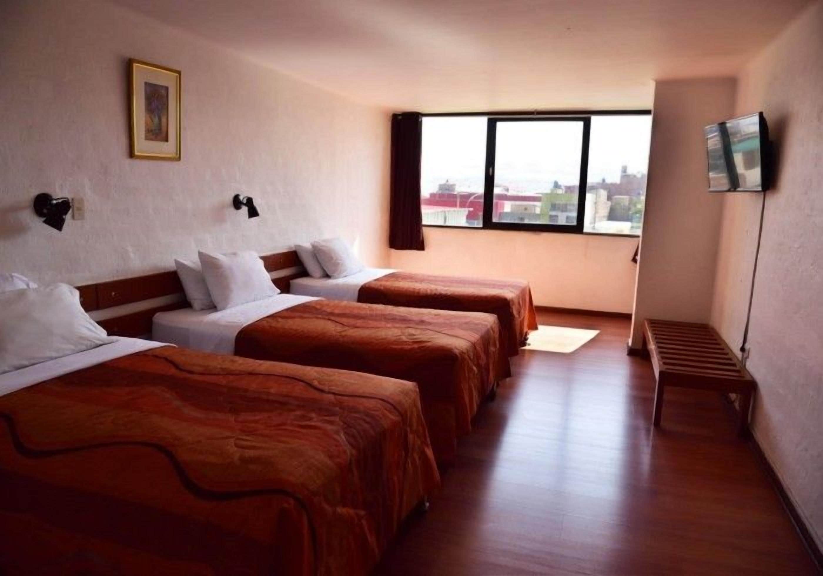 Quarto de hotel com três camas, televisão e uma janela grande.