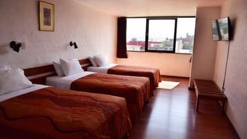 Quarto de hotel com três camas, televisão e uma janela grande.