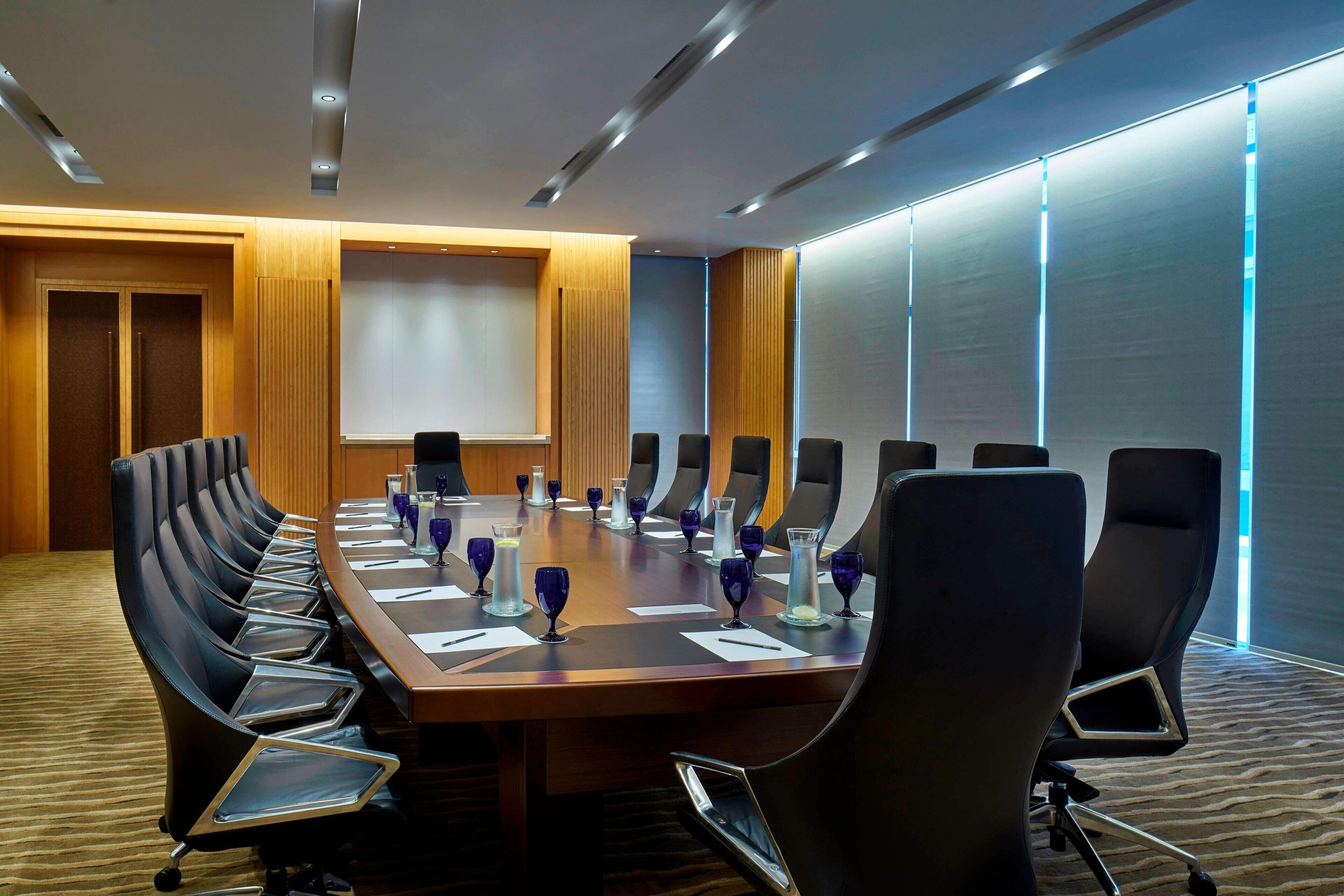 Uma sala de conferências com uma mesa comprida, várias cadeiras e uma tela de projeção.