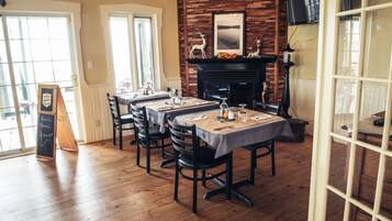 Uma sala de jantar com piso de madeira, lareira e mesa posta para quatro pessoas.
