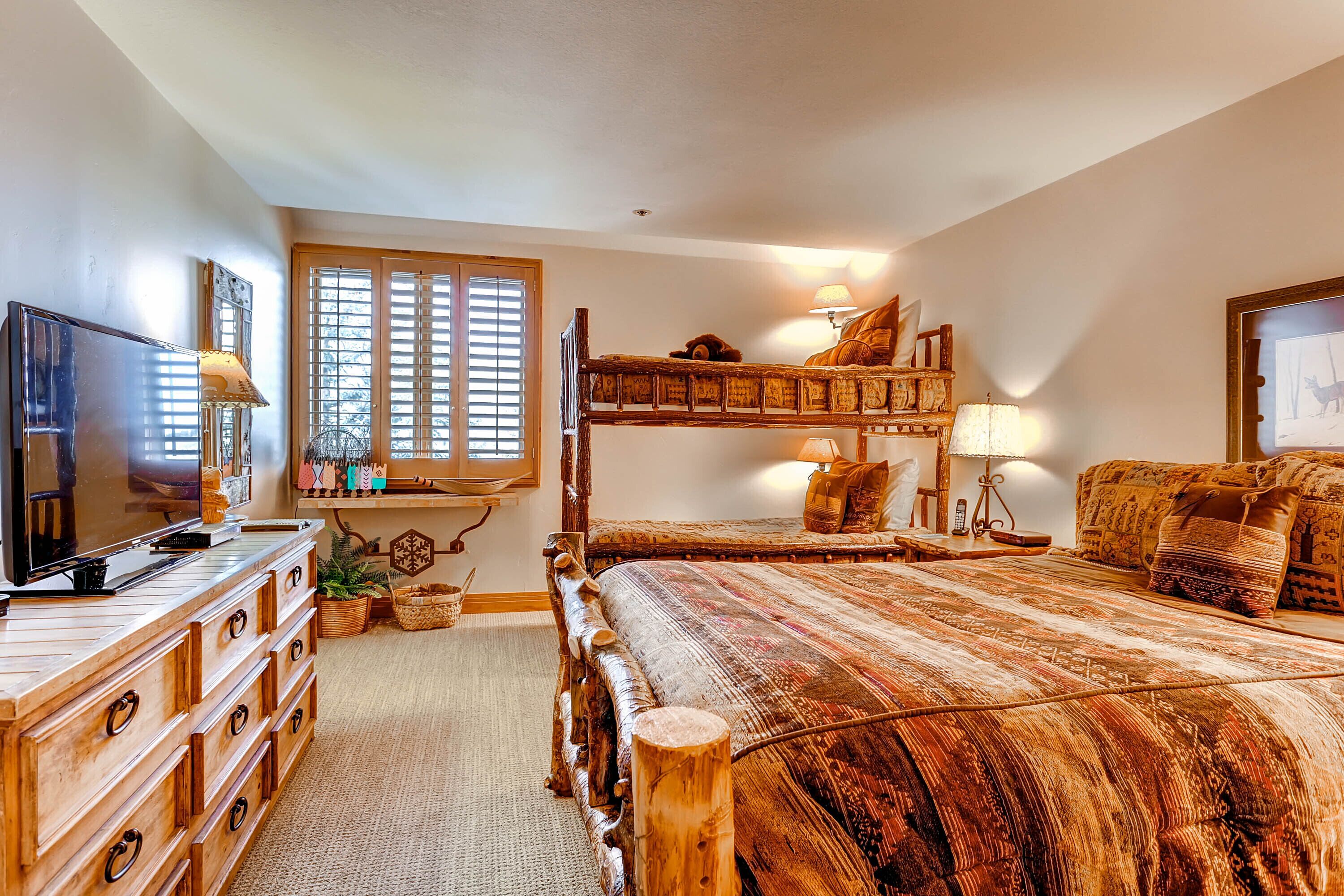 Um quarto aconchegante com uma cama grande, televisão, móveis de madeira e janela com persianas.