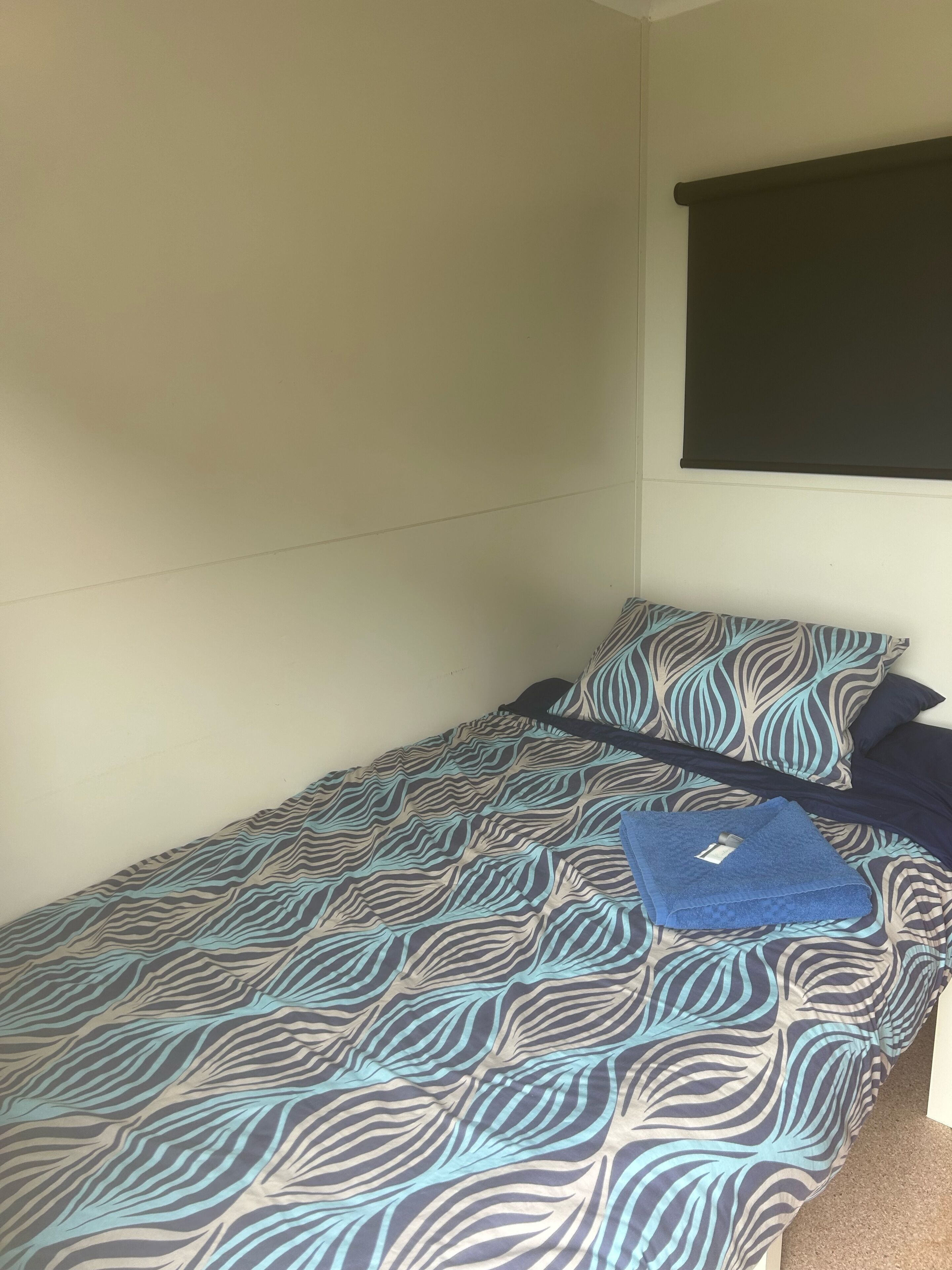 Quarto pequeno com uma cama de solteiro, edredom estampado com padrão de zebra, cabeceira escura e janela com persiana.