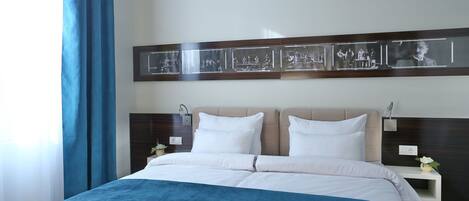 Quarto de hotel com cama, mesa de cabeceira, painel de fotos na parede e janela com cortinas.