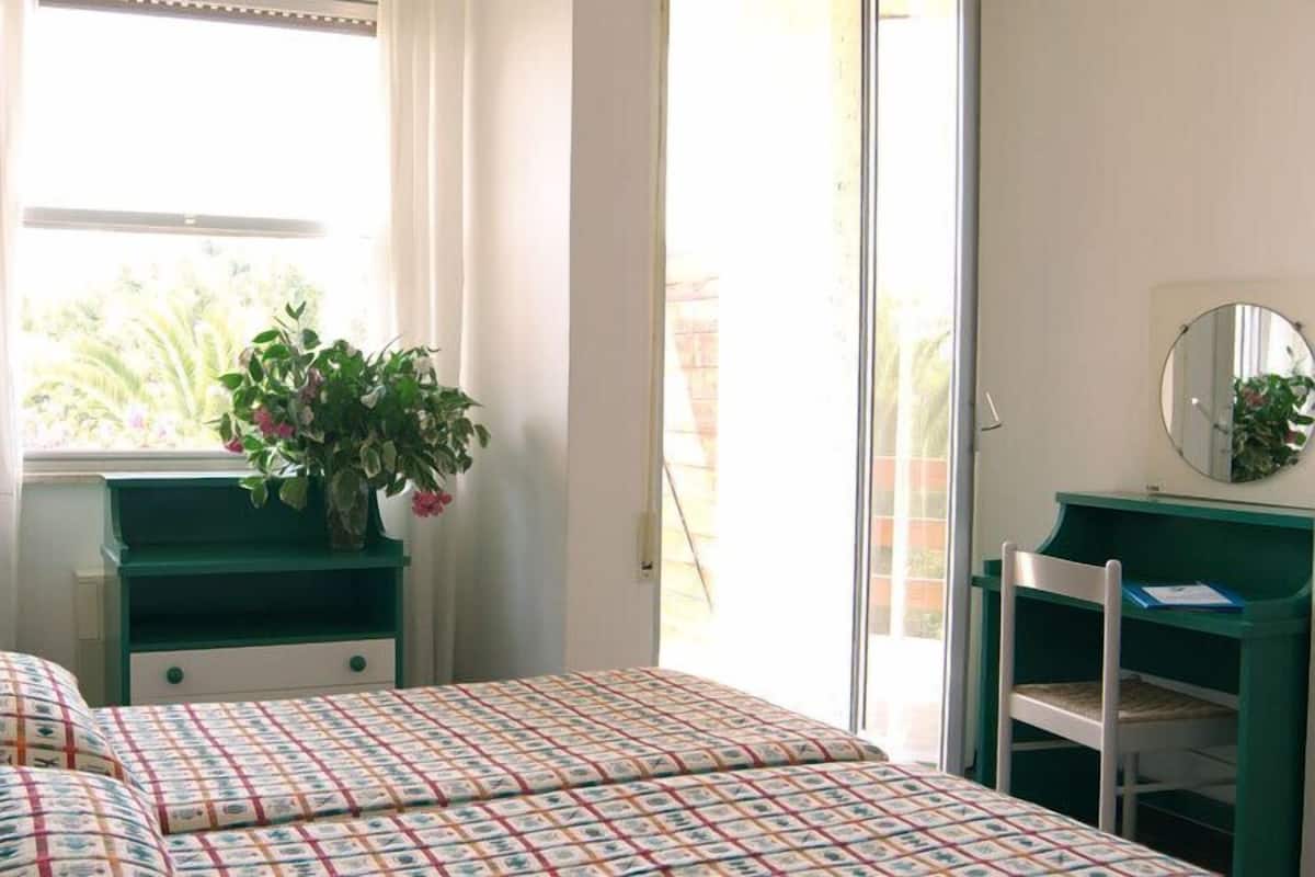 Um quarto com cama, cômoda, cadeira, espelho e janela com cortinas.